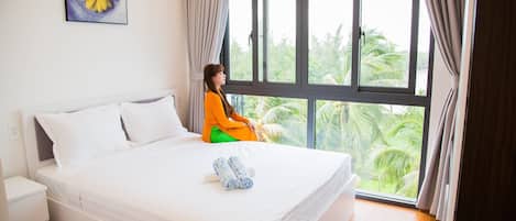 Quarto com uma janela grande, cama com roupa de cama branca e um quadro de uma flor na parede.