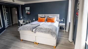 Quarto moderno com uma cama grande, mesas de cabeceira, escrivaninha e uma cadeira.