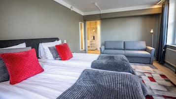 Quarto de hotel com cama, sofá cinzento e vista para um corredor.
