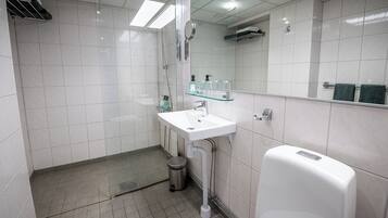 Uma casa de banho moderna com uma sanita branca, prateleiras de vidro, um espelho e uma área de duche.