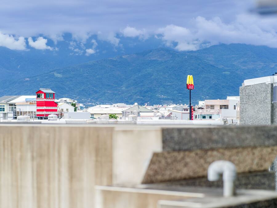 Vista de uma cidade costeira com um prédio vermelho e branco notável, um letreiro do McDonald's e uma montanha ao fundo.