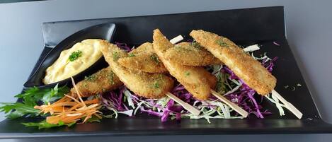 Um prato com petiscos empanados e fritos, possivelmente tiras de frango, acompanhado de salada de repolho e um molho cremoso para molhar.