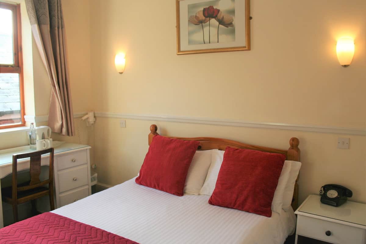 Quarto de hotel bem arrumado, com uma cama, uma escrivaninha e uma cadeira.