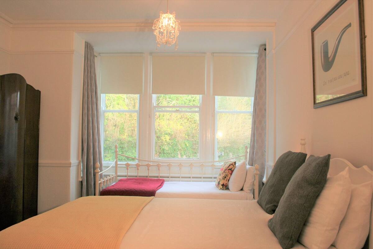 Quarto com cama grande, janela com cortinas, lustre e quadro na parede.