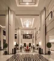Um hall de hotel moderno com um piso estampado em padrão geométrico, uma área de estar central e um alto teto com iluminação embutida.