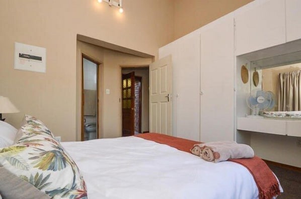 Quarto de hotel com cama, espelho, guarda-roupa e porta de acesso a um banheiro.