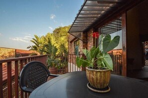 Uma área de pátio com mesa redonda e cadeiras, cercada por vasos de plantas e um muro de tijolos.
