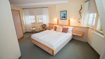 Quarto de hotel com uma cama de solteiro, mesas de cabeceira, uma cadeira, uma pequena mesa e uma janela com cortinas.