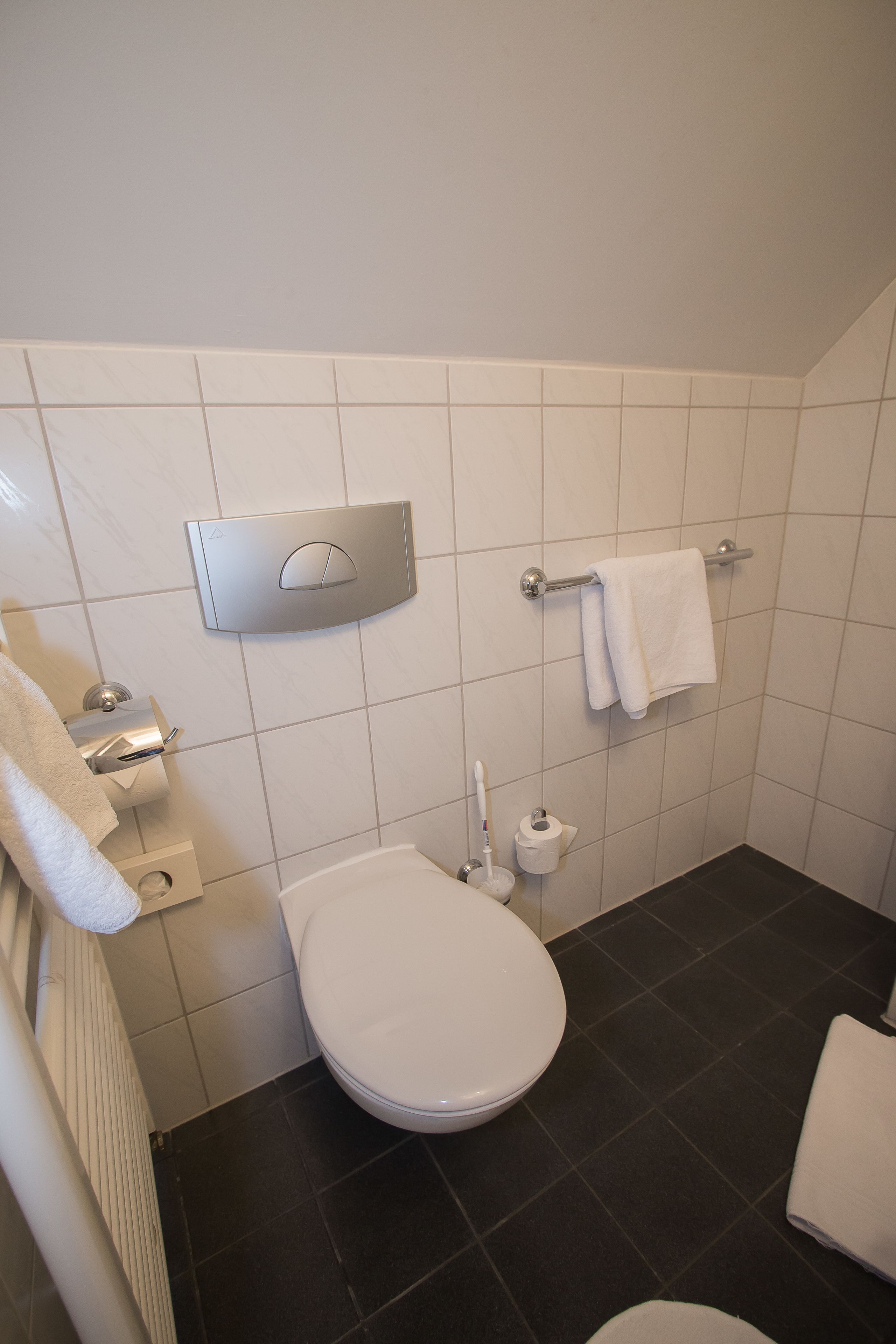 Um banheiro moderno com vaso sanitário branco, porta-toalhas, dispensador de papel toalha e suporte para papel higiênico.