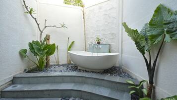 Um banheiro moderno com uma banheira independente, degraus que levam a uma pequena área de estar e diversas plantas.