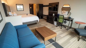 Quarto de hotel com uma cama, uma escrivaninha com cadeira, um sofá e uma mesa pequena.