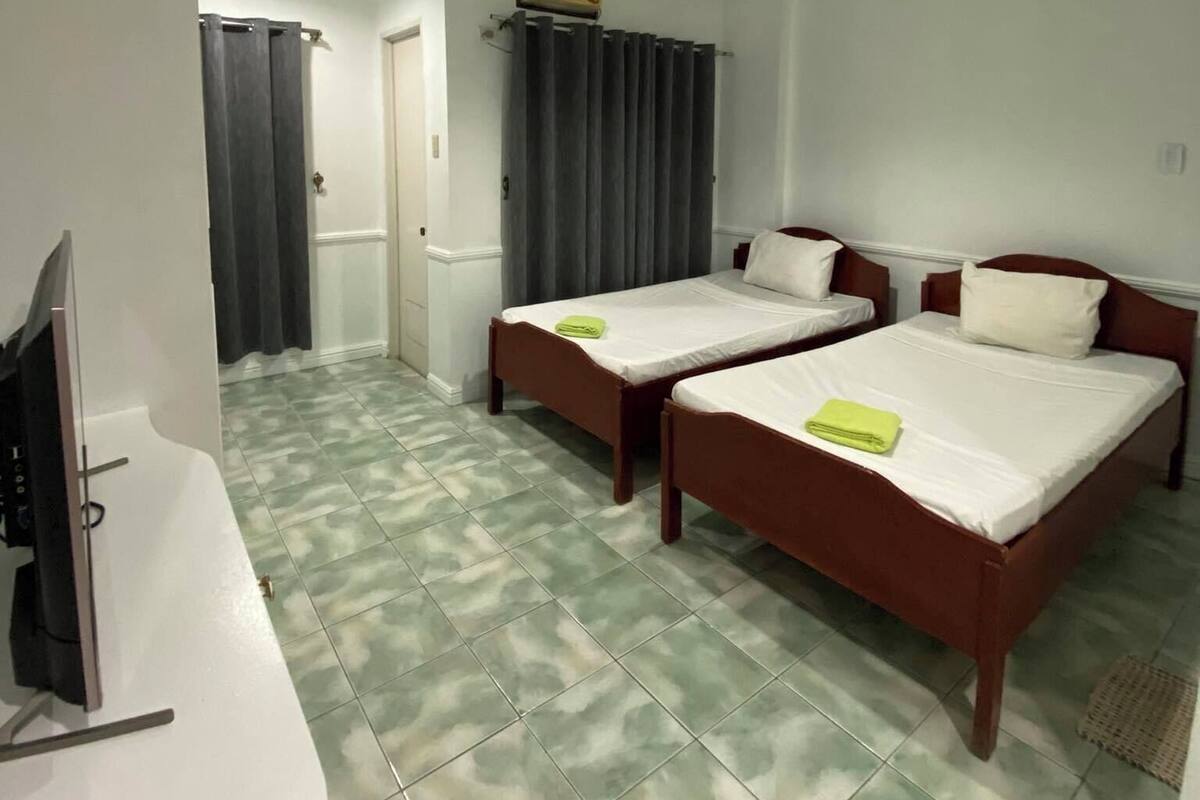 Quarto de hotel com duas camas, televisão e banheiro com cortina de chuveiro.