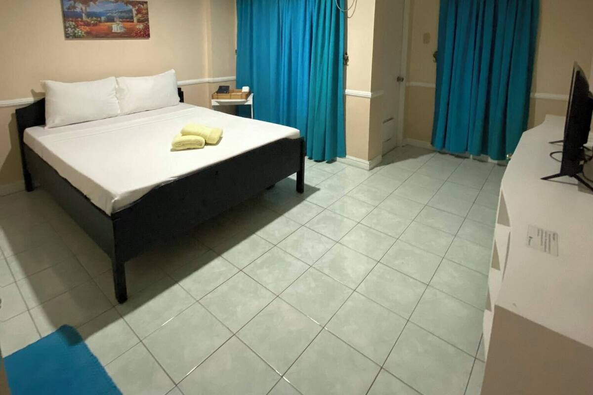 Quarto de hotel com cama, escrivaninha, cadeira, pintura na parede e banheiro com cortina de chuveiro.
