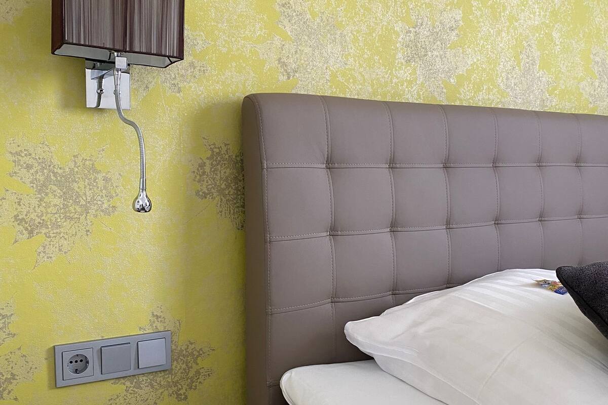 Quarto com cama, mesa de cabeceira e luminária na parede.