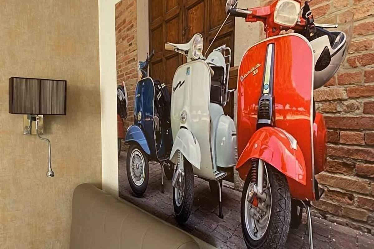 Quarto com um mural de scooters antigas, uma cama e um candeeiro fixado na parede.