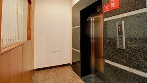 Interior de elevador com painel digital, aviso de proibido fumar e sinal de alerta de vigilância.