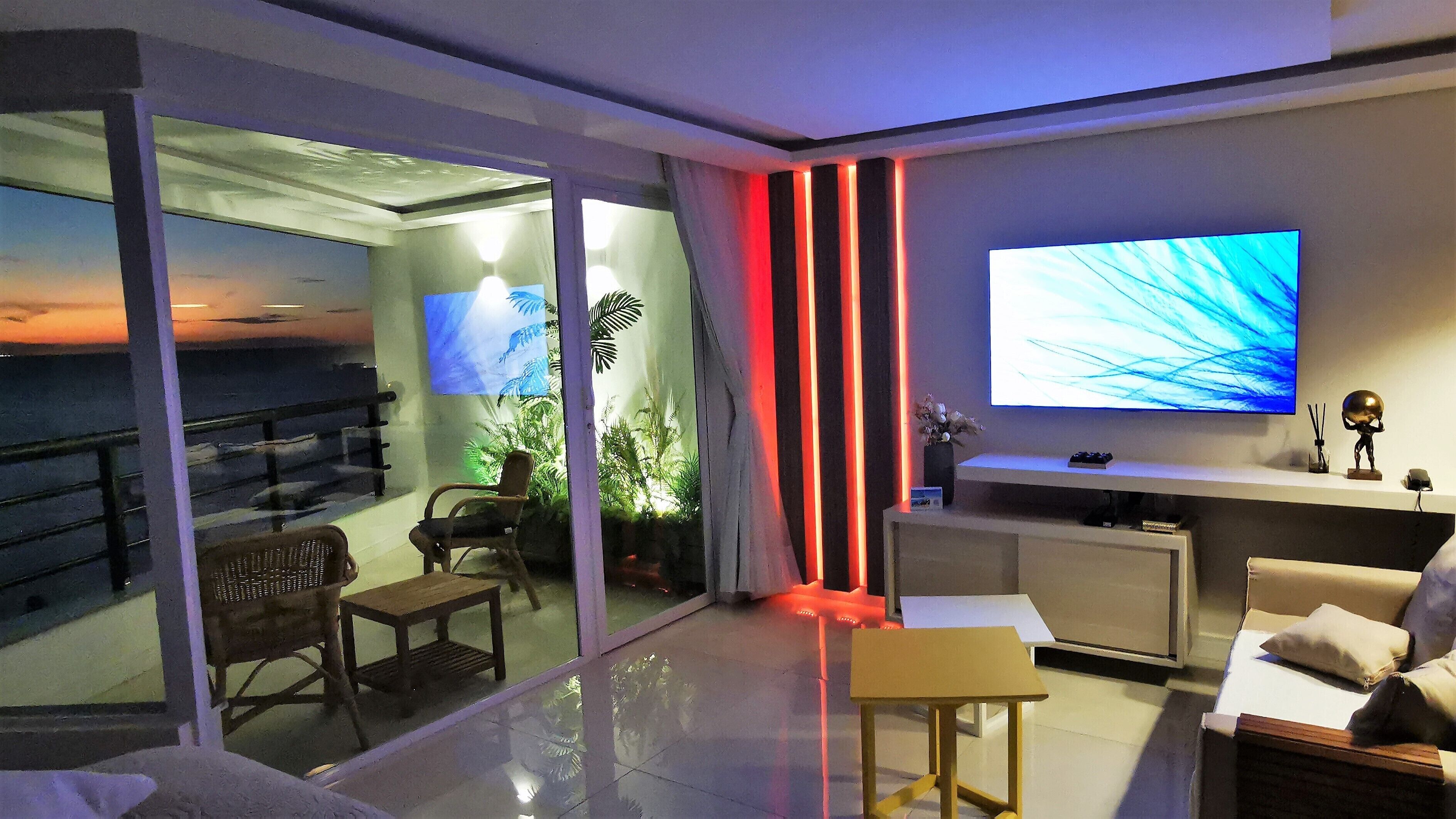 Uma sala de estar moderna com uma televisão grande, um sofá, uma mesa de centro e uma varanda com vista.