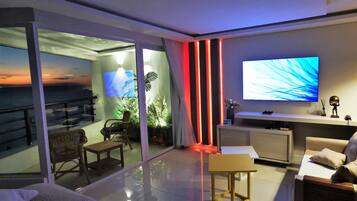 Uma sala de estar moderna com uma televisão grande, um sofá, uma mesa de centro e uma varanda com vista.