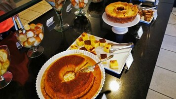 Uma mesa de buffet com diversos doces, incluindo uma torta grande, pequenos bolinhos quadrados e um bolo bundt.