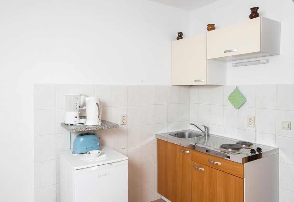 Uma cozinha compacta com fogão pequeno, cafeteira e micro-ondas.
