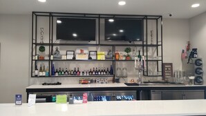Uma área de bar com prateleiras de garrafas de bebidas, uma televisão montada acima e um caixa no balcão.