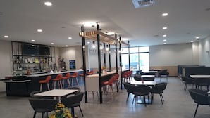 Um restaurante moderno com área de bar, diversas opções de assento incluindo mesas e cabines, e uma grande janela que proporciona luz natural.