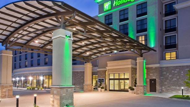 Entrada de um hotel Holiday Inn, com galeria coberta, vários acessos e uma placa verde destacada.