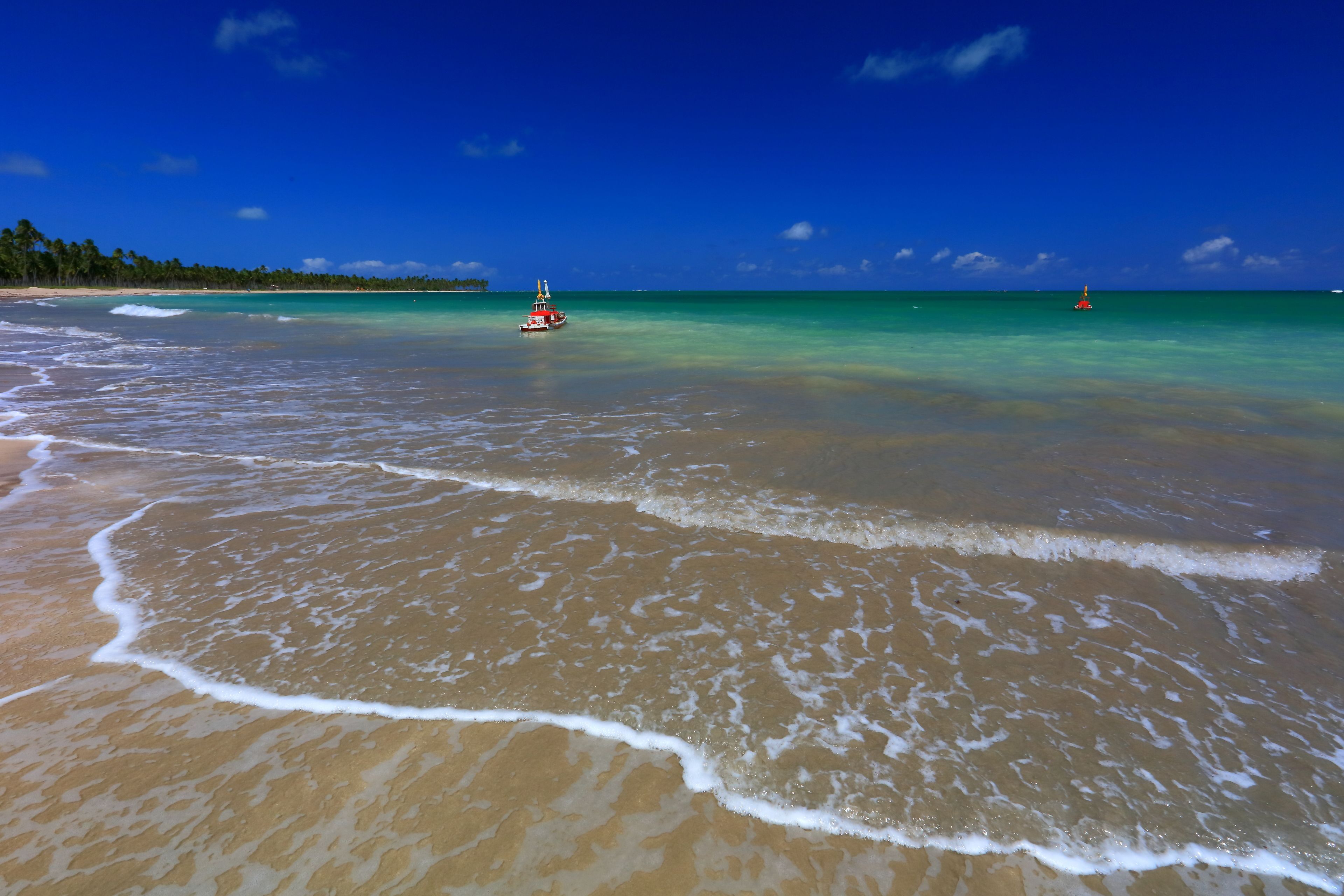 Uma praia com águas turquesa cristalinas, um barco vermelho e uma ilha ao longe.