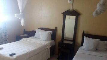 Quarto de hotel com duas camas, uma mesa de cabeceira, um espelho e um ventilador de teto.