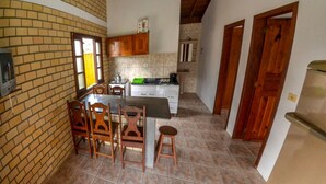 Cozinha com parede de tijolos, armários de madeira, piso ladrilhado e área de refeições com cadeiras e bancos.