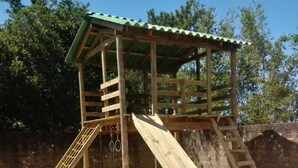Uma estrutura de recreação de madeira com telhado, escorregadores e uma escada.