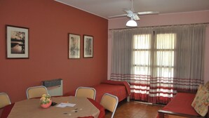 Quarto com mesa de jantar, cadeiras, cama e janela com cortinas.