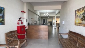 Uma área de recepção com um banco de madeira, um extintor de incêndio vermelho e um balcão de atendimento.