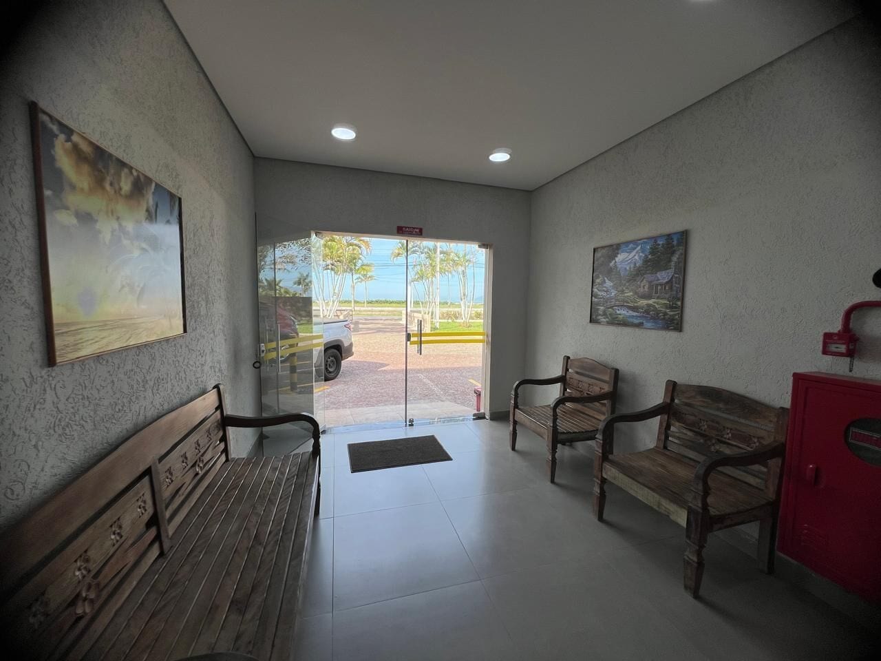 Uma área de recepção com dois bancos de madeira, um armário de arquivo vermelho e uma porta de vidro que dá para o exterior.