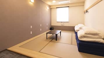 Quarto com piso de tatame, uma mesa baixa, cama com roupa de cama branca e janela com persianas.