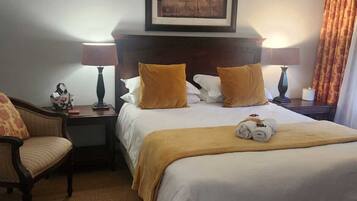 Quarto de hotel com uma cama grande, duas mesas de cabeceira com luminárias, uma cadeira, ar condicionado e uma obra de arte emoldurada na parede.