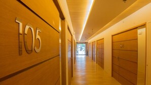 Um corredor com painéis de madeira e portas numeradas, dando acesso a quartos individuais.