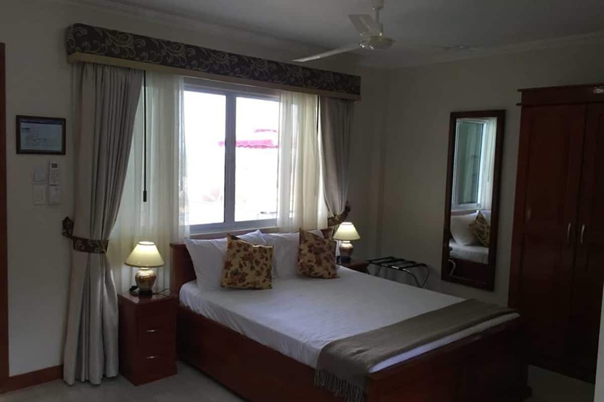 Quarto com uma cama grande, duas mesas de cabeceira com luminárias, um ventilador de teto e uma janela com cortinas.
