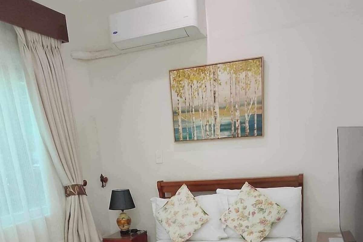 Quarto com cama, mesa de cabeceira, luminária, pintura e ar condicionado.