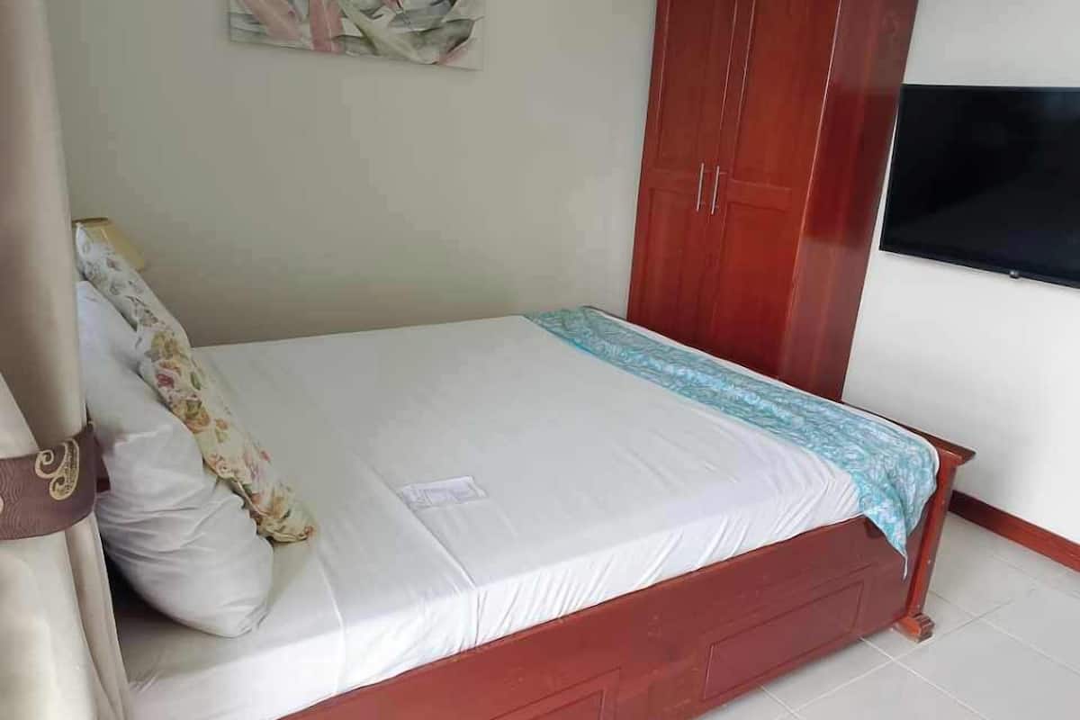 Quarto com cama, guarda-roupa de madeira e televisão na parede.