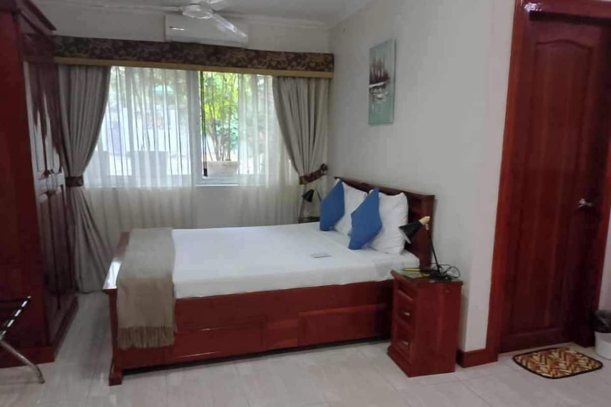 Um quarto bem arrumado com cama, mesa de cabeceira e janela com cortinas.