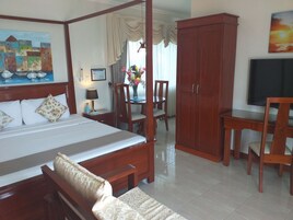 Quarto de hotel com cama de dossel, mobiliário de madeira, escrivaninha e televisão.