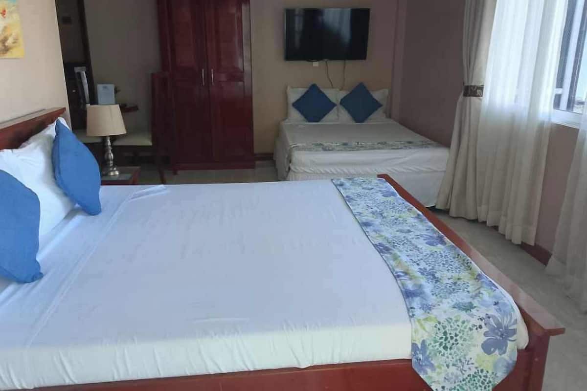 Quarto de hotel com uma cama grande, uma cama menor, um guarda-roupa, uma televisão e uma janela com cortinas.