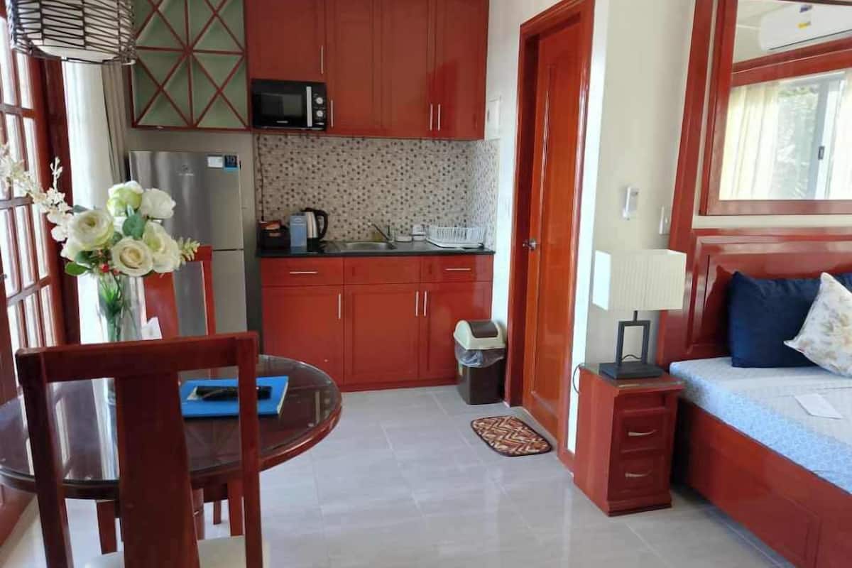Quarto compacto com cama, pequena escrivaninha, mesa de refeições e cozinha compacta.