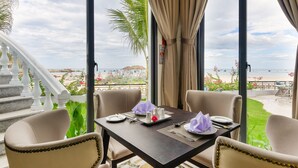 Uma área de refeições com uma mesa posta para dois, com vista para uma praia e para o oceano, e um parque de diversões ao longe.