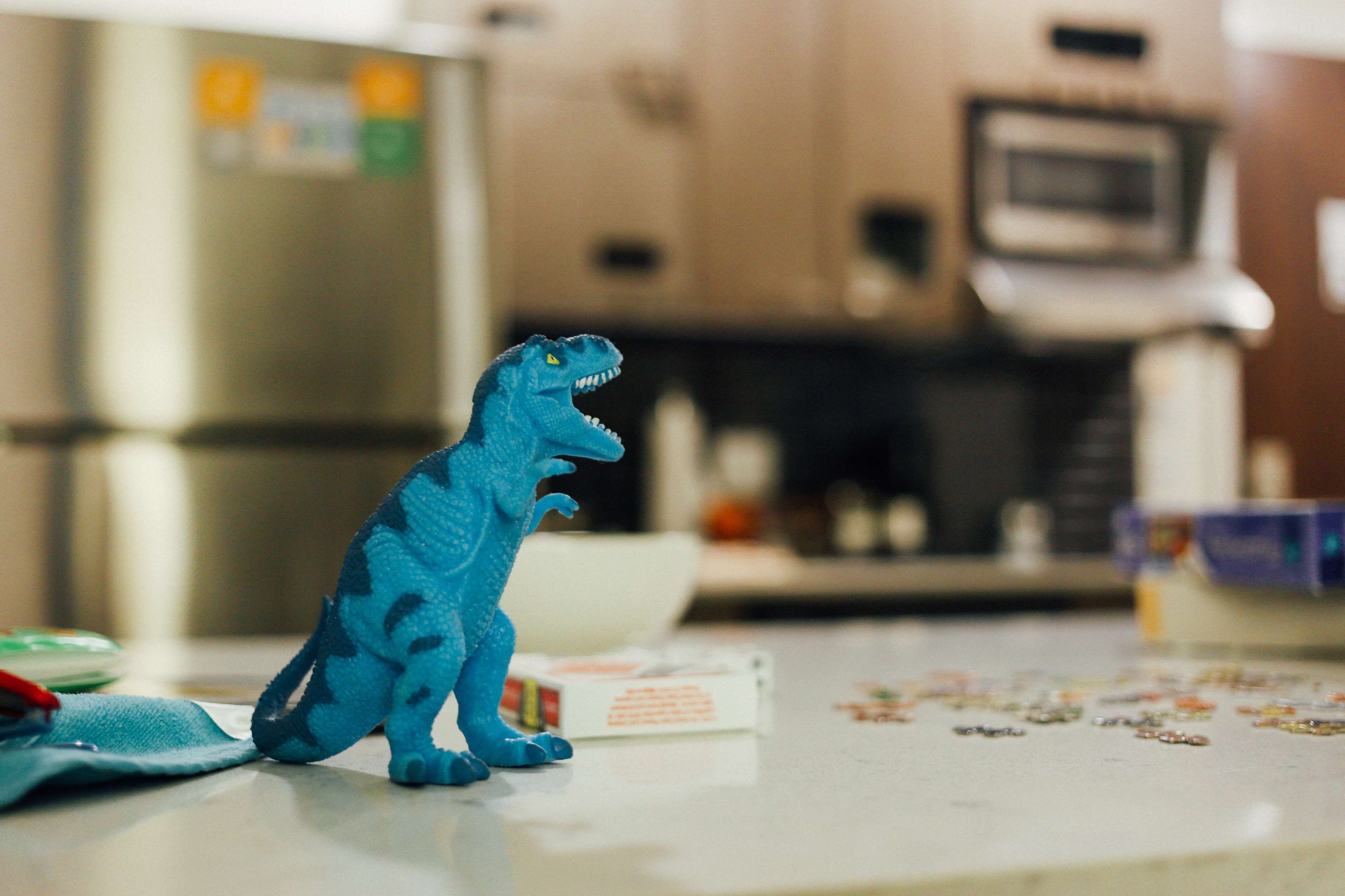 Um brinquedo de dinossauro em uma bancada de cozinha, com fundo desfocado.