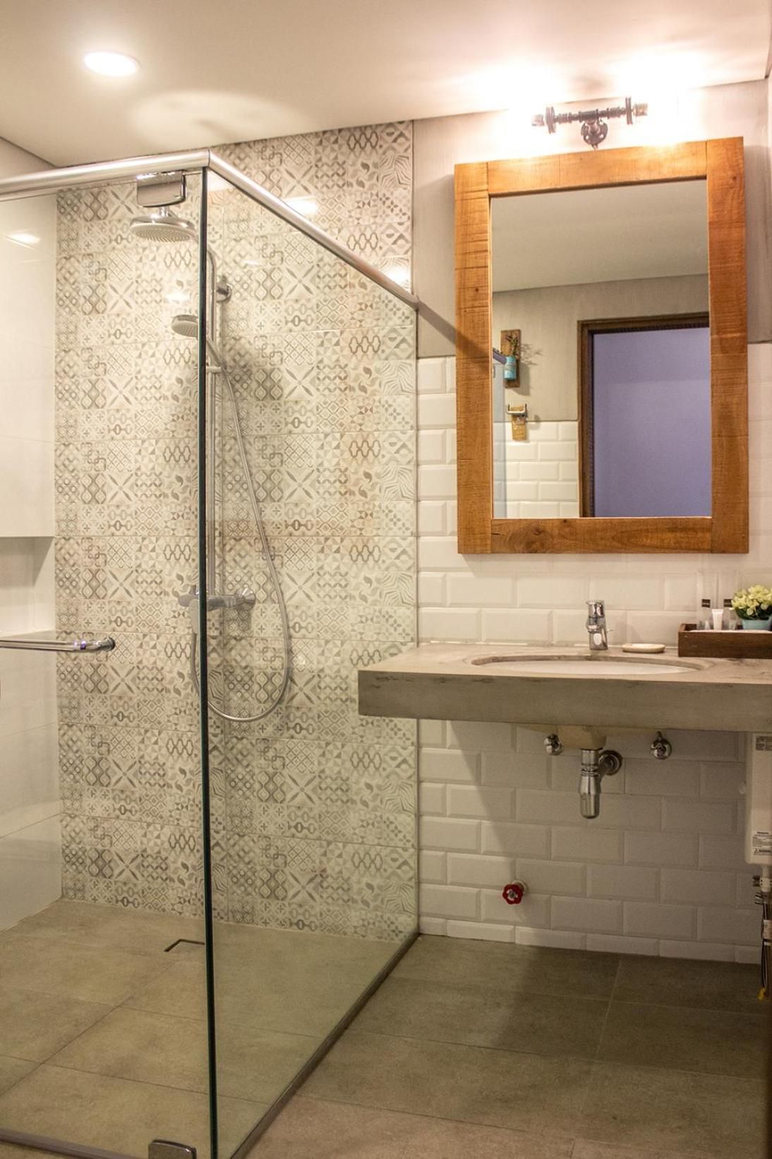Casa de banho com cabine de duche em vidro, espelho com moldura de madeira e zona de lavatório revestida a azulejos brancos.