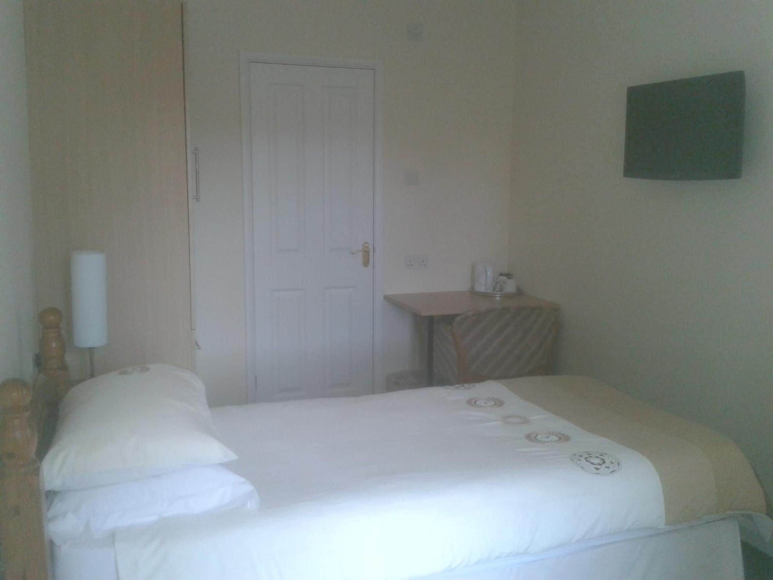 Quarto com cama, mesa de cabeceira, luminária e porta.