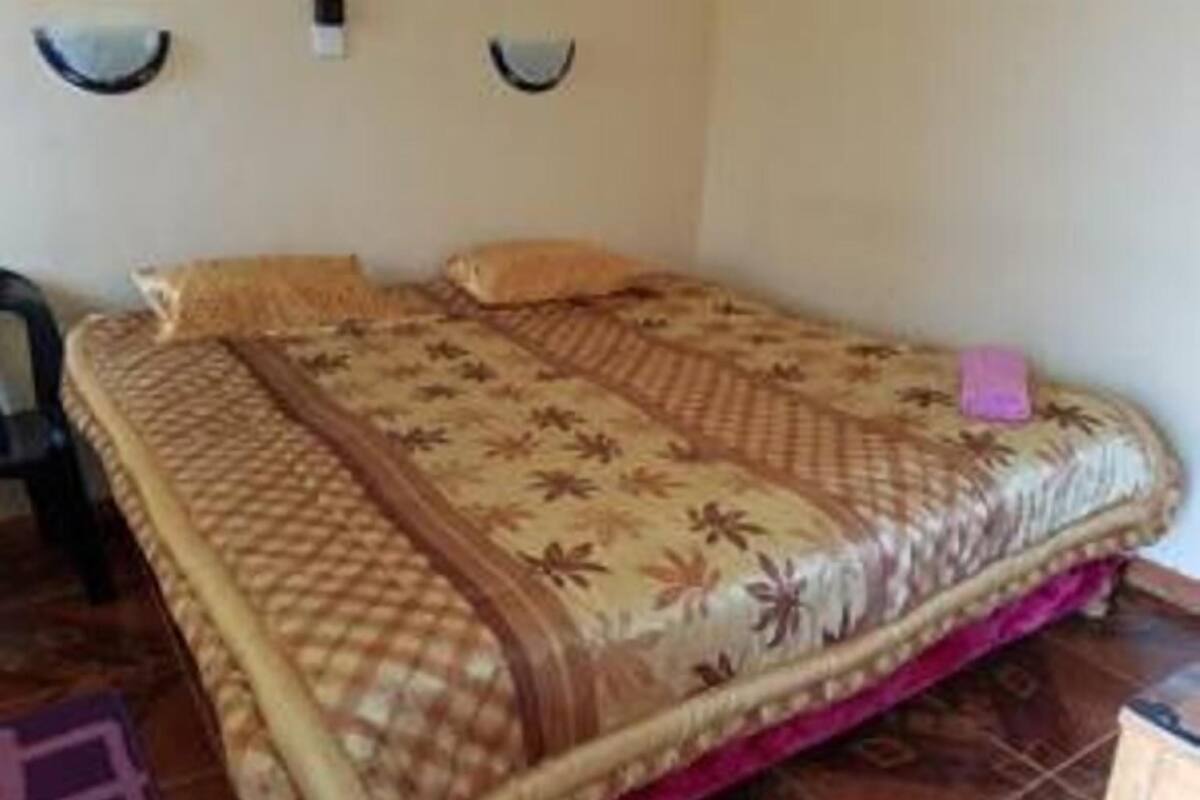 Uma cama com colcha estampada, um travesseiro rosa e uma cadeira preta num quarto com piso de azulejos.