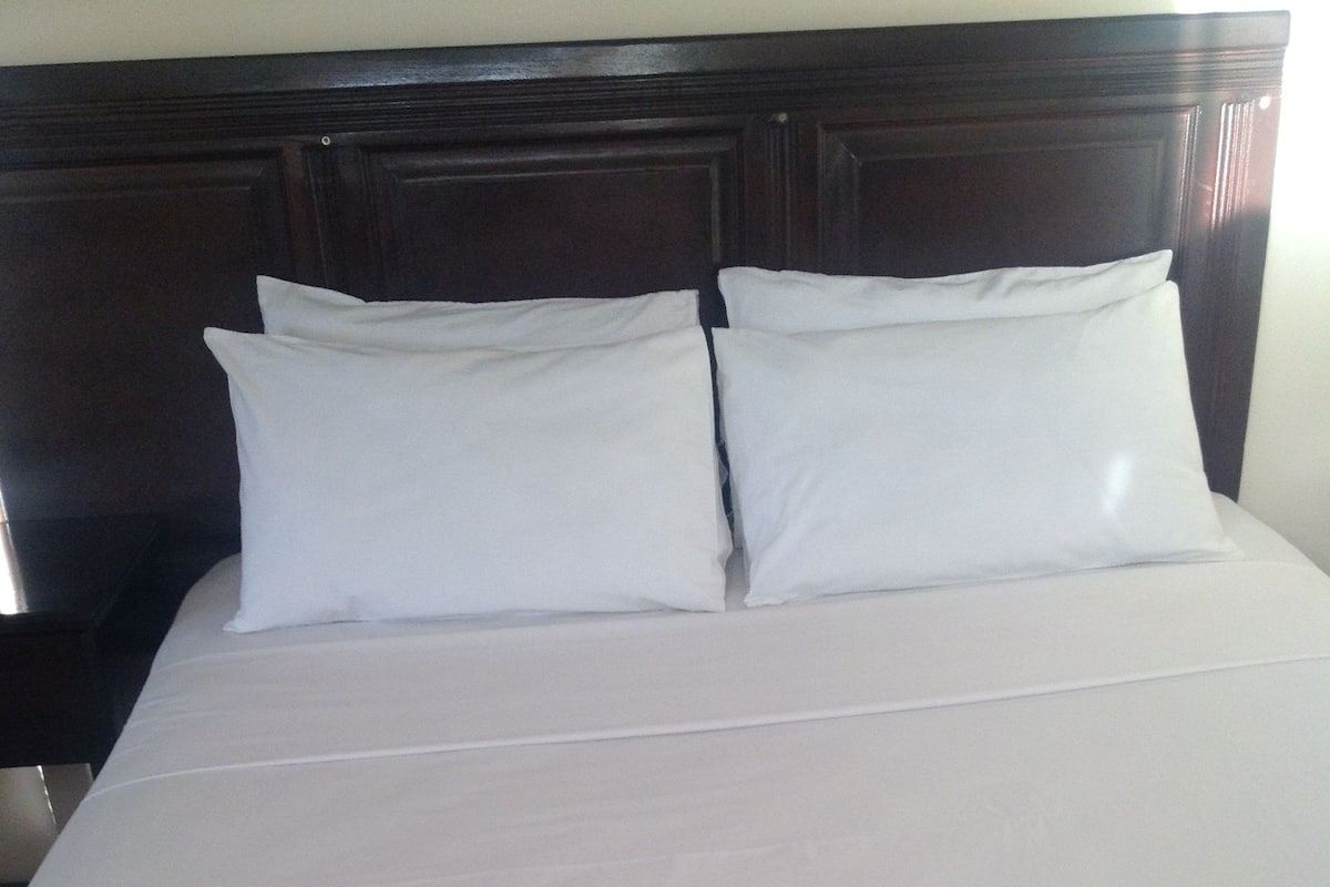 Cama bem arrumada com cabeceira de madeira e roupa de cama branca.